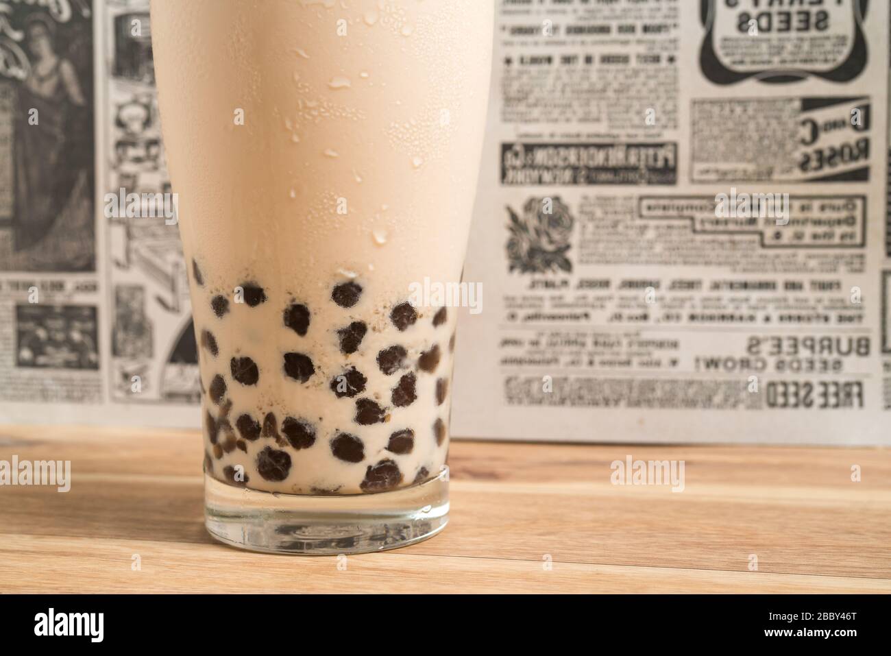 A glass cup of pearl milk tea (also called bubble tea) and a plate of tapioca ball on wooden ...