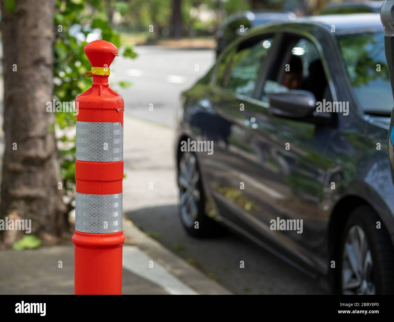 Skinny orange safety cone on sidewalk near street parking cars Stock ...