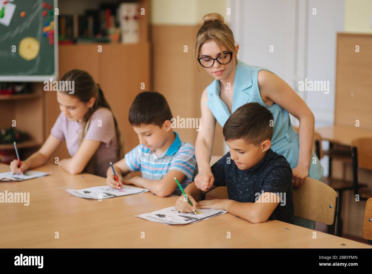 Teacher helping school kids writing test in classroom. education ...