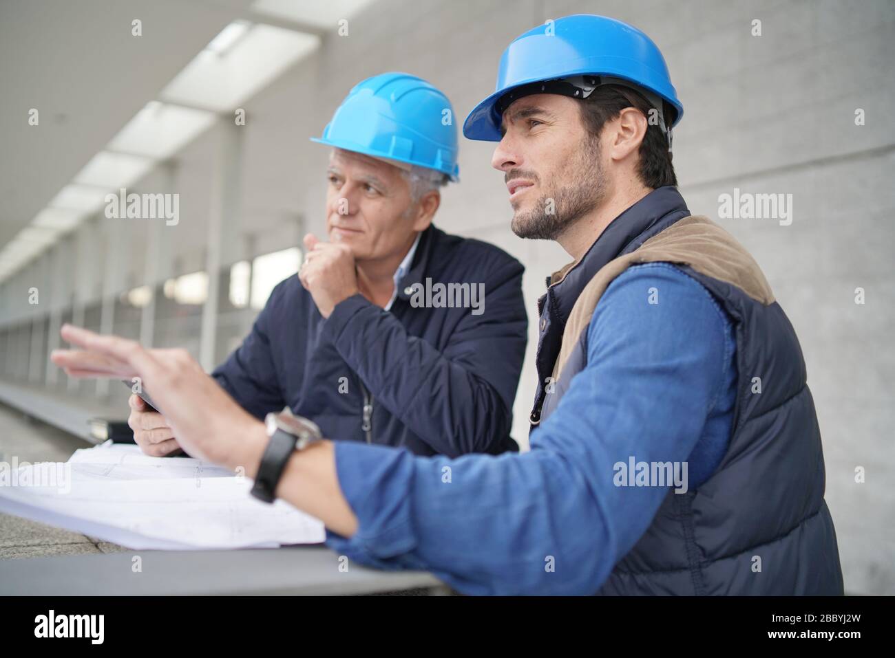 Workmen consulting over blueprint on modern building sight Stock Photo ...