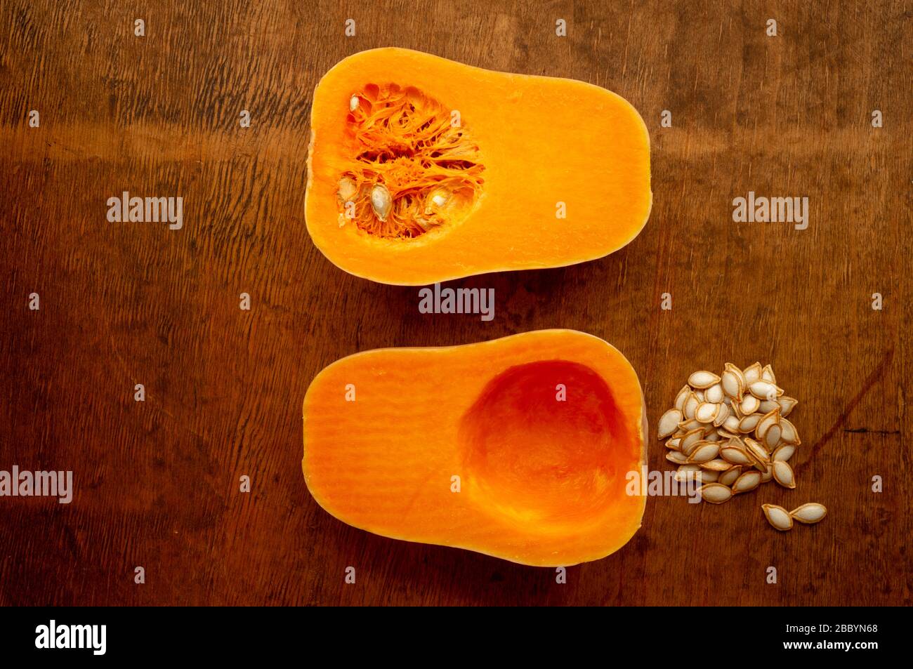 Two halves of sliced ripe butternut squash with seeds on rustic wooden ...