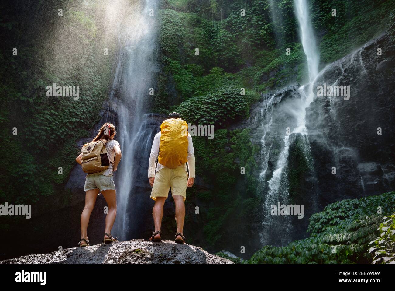 Couple of travelers or hikers with backpacks are standing on big rock ...