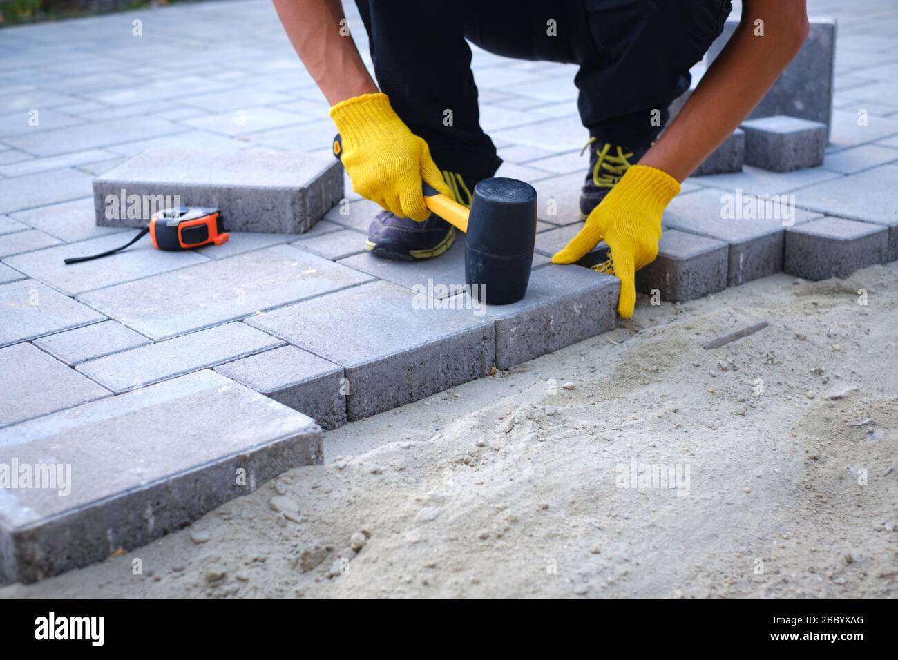 The master in yellow gloves lays paving stones in layers. Garden brick ...