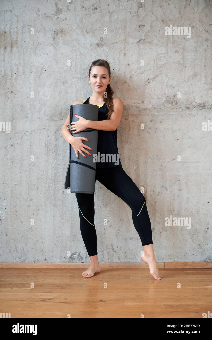 Front view of positive young sporty girl holding mat, standing and ...