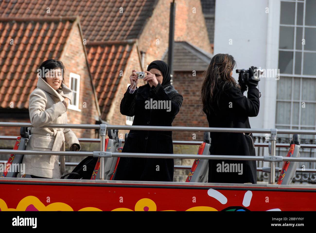Three Muslim tourists on the top deck of a city sight-seeing tour bus ...