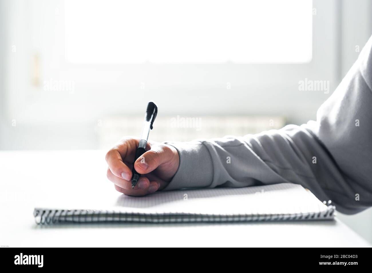 Young man writing in a notebook doing homework at his desk at home ...