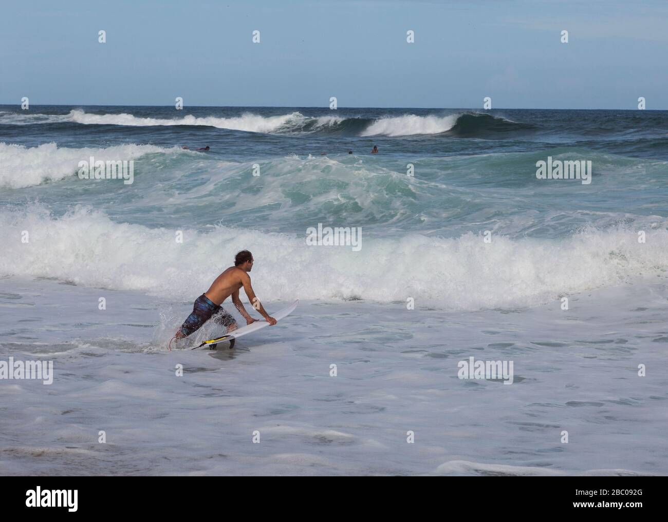 A surfer runs into the waves with surfboard on the beaches of Rio de ...