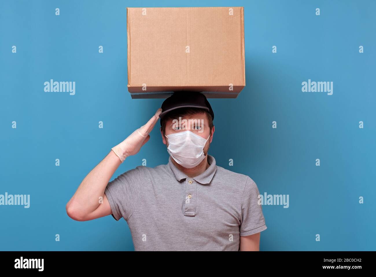 Young delivery man in medical mask holding and carrying a cardbox ...