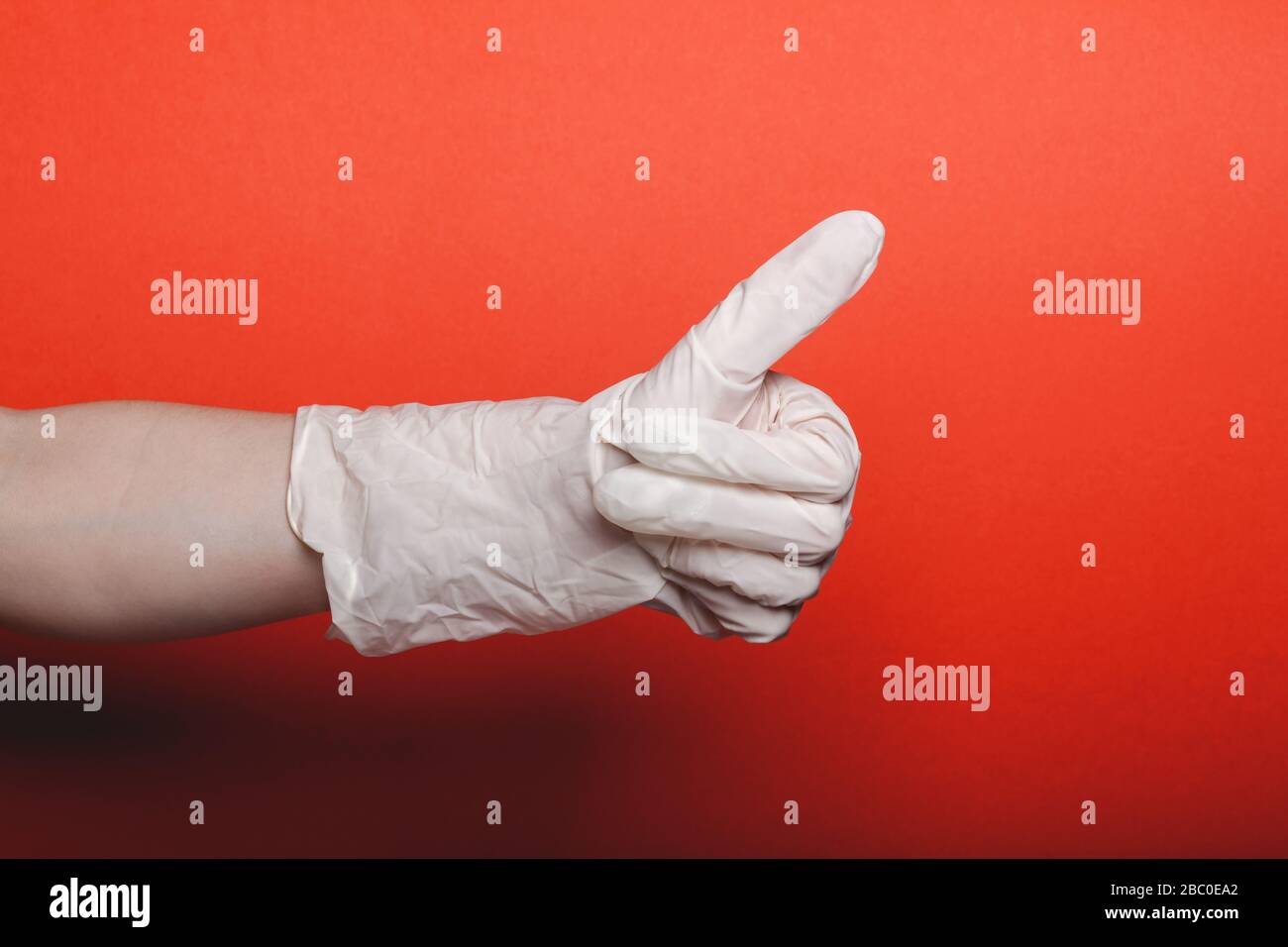 Child hand in big medical glove shows thumb up on red background, place ...