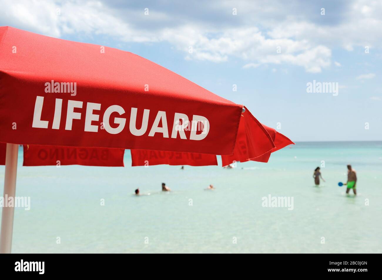 Red lifeguard umbrella on a beach against blue sky. Some bathers ont he ...