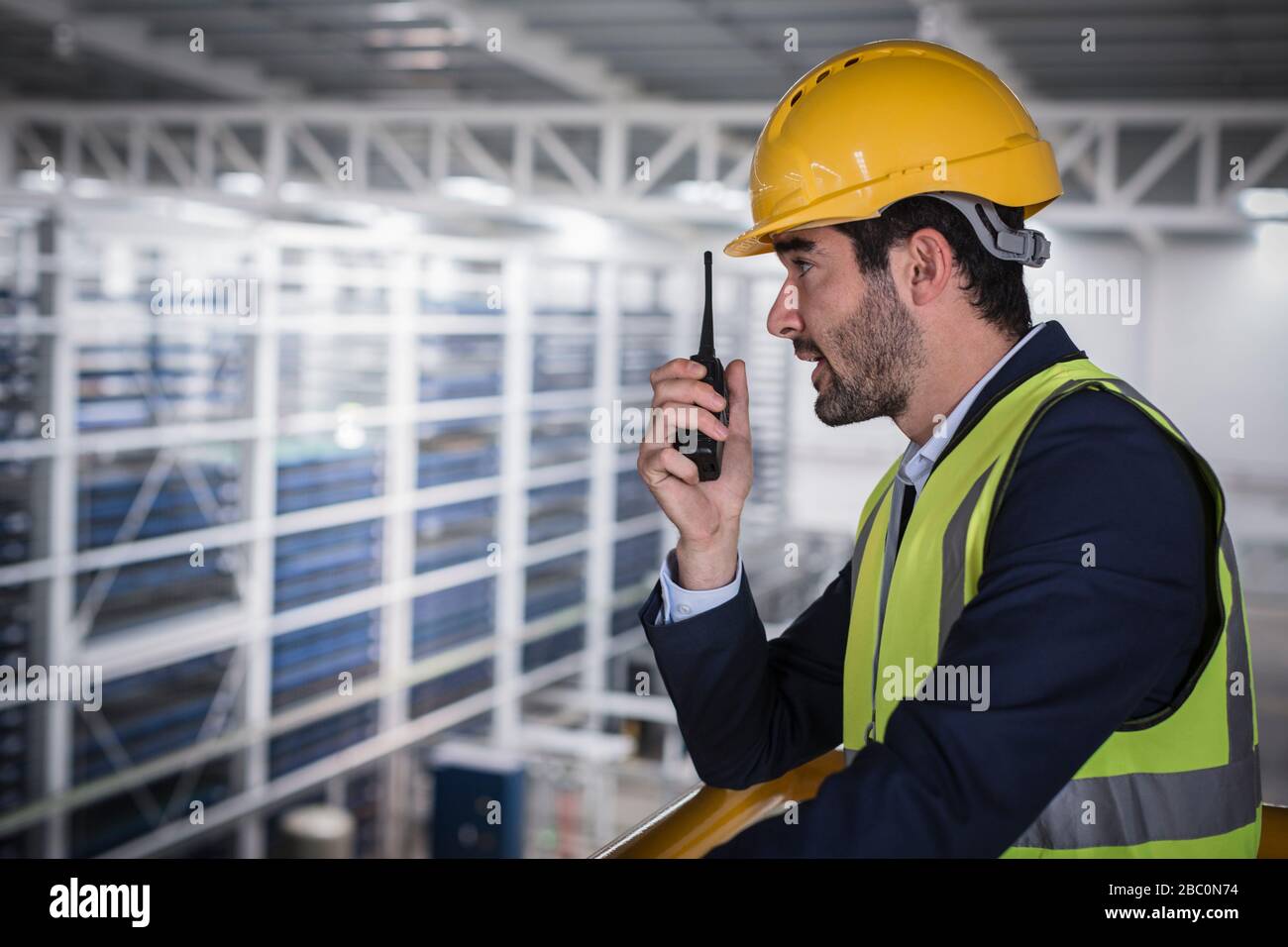 Male supervisor talking, using walkie-talkie on platform in factory ...