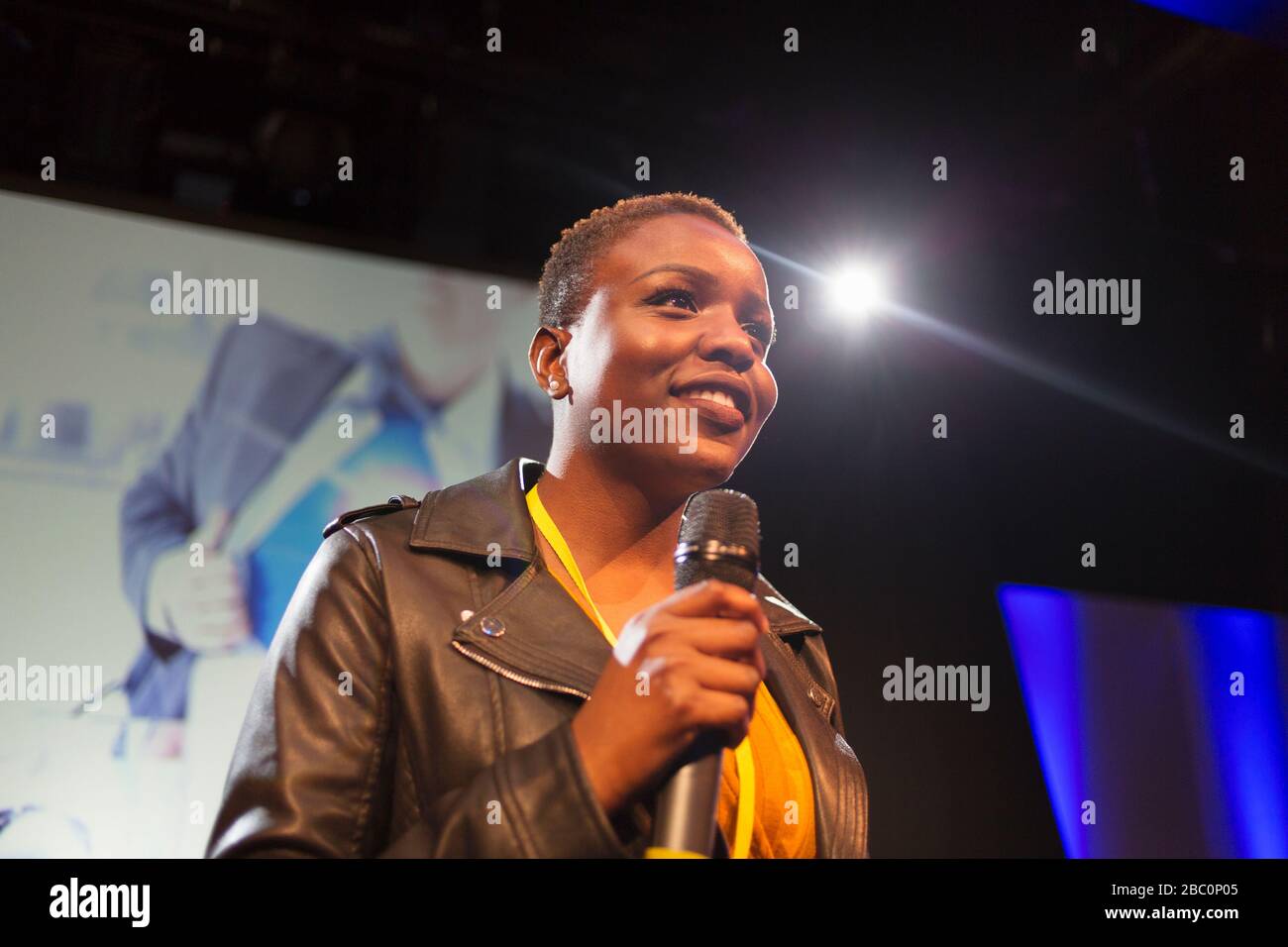 Smiling female speaker with microphone on stage Stock Photo - Alamy