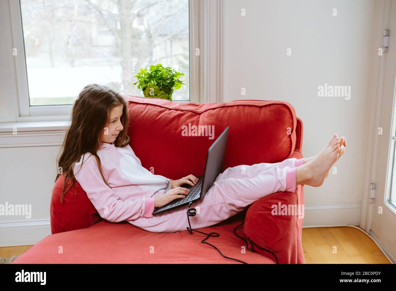 Preteen girl enjoyes homeschooling in comfy pajama and cozy sofa chair ...