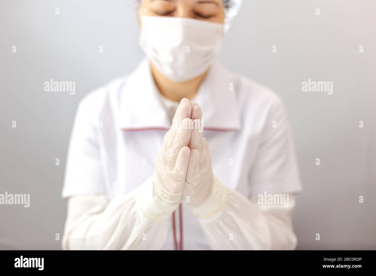 The assistant or doctor with mask and gloves stand in prayer to ...