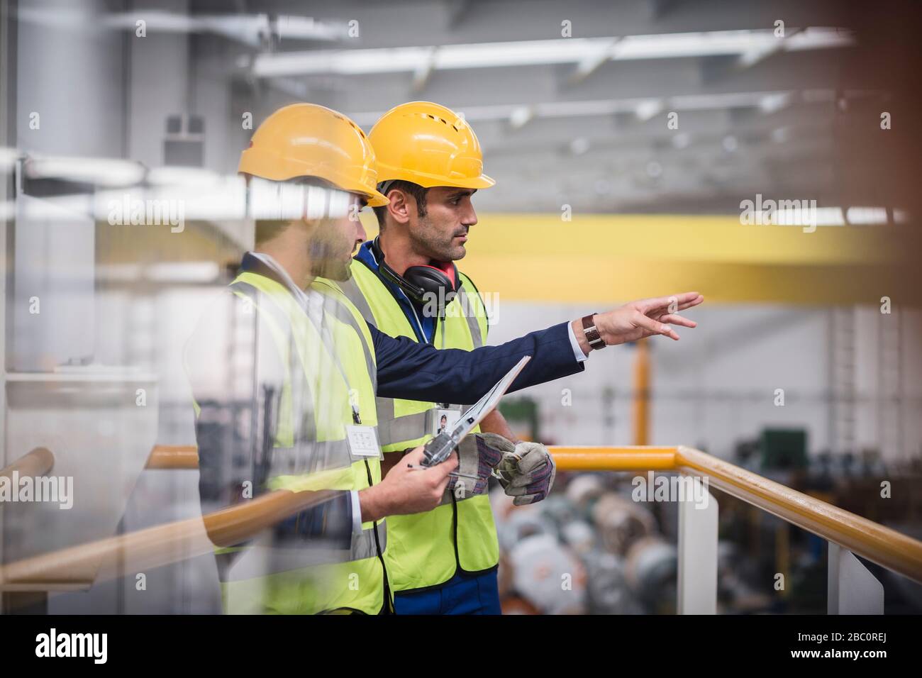 Male supervisors with clipboard talking on platform in factory Stock ...