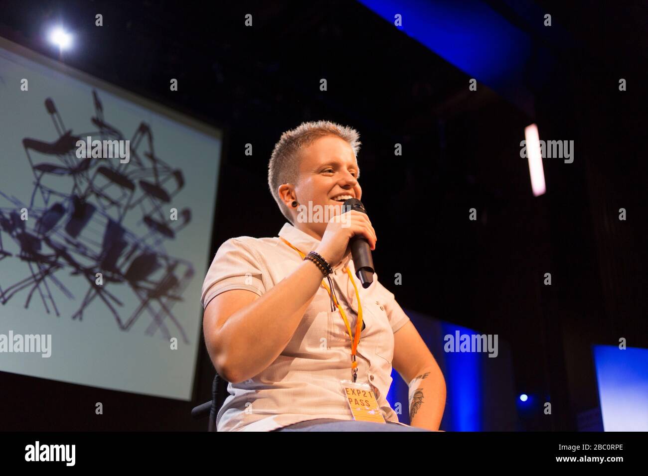 Smiling female speaker with microphone on stage Stock Photo - Alamy