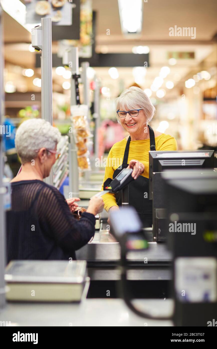 Senior female cashier helping customer at supermarket checkout Stock ...