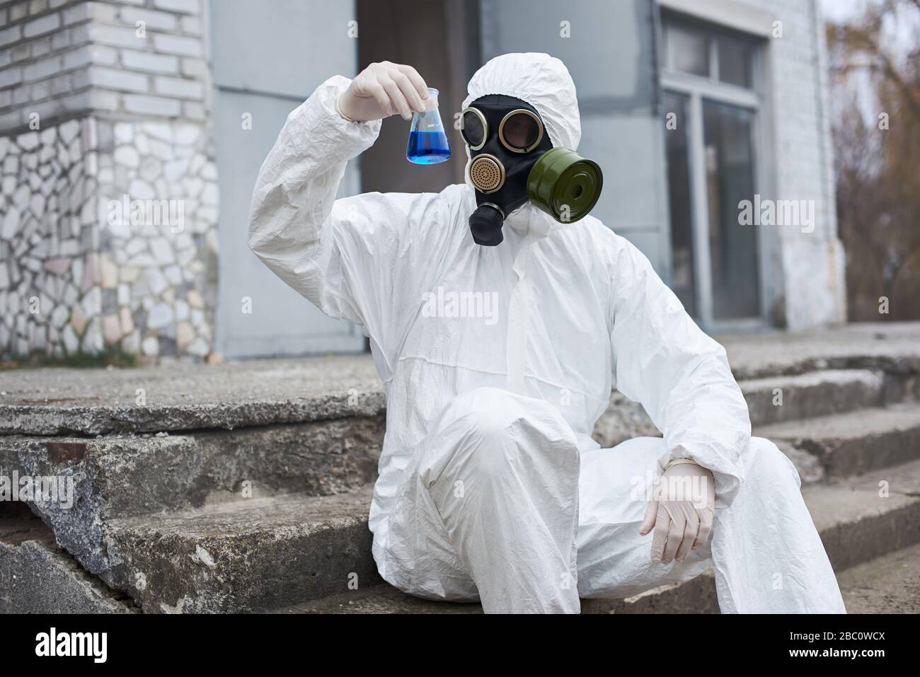 Scientist wearing protective uniform and gas mask, sitting on the ...
