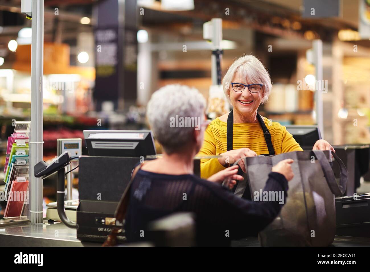 Friendly senior female cashier helping customer supermarket checkout ...