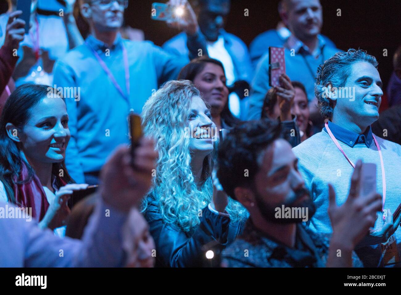 Smiling woman with camera phone in dark audience Stock Photo - Alamy