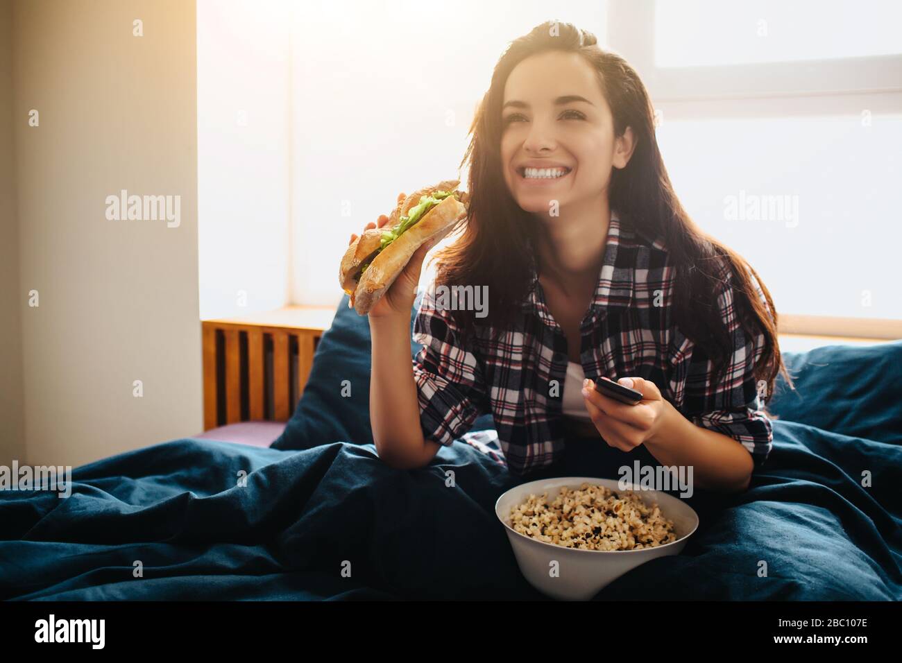 Young beautiful woman in morning bed at home. Watch tv or movie and use ...