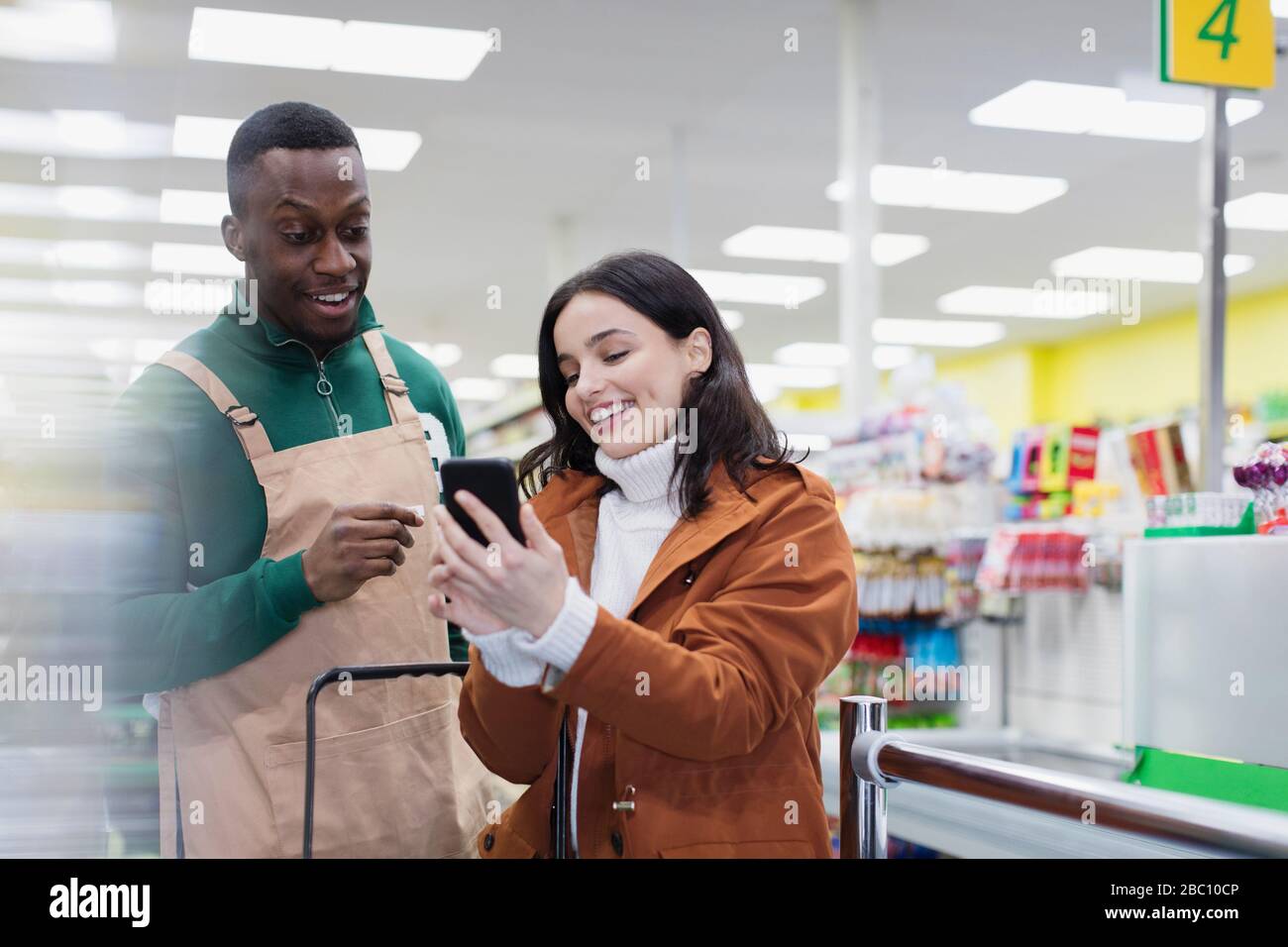 Grocer helping customer with smart phone in supermarket Stock Photo - Alamy