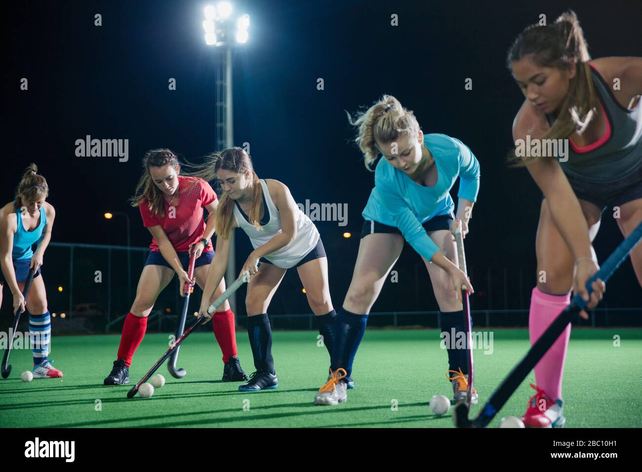 Focused young female field hockey players practicing sports drill on ...