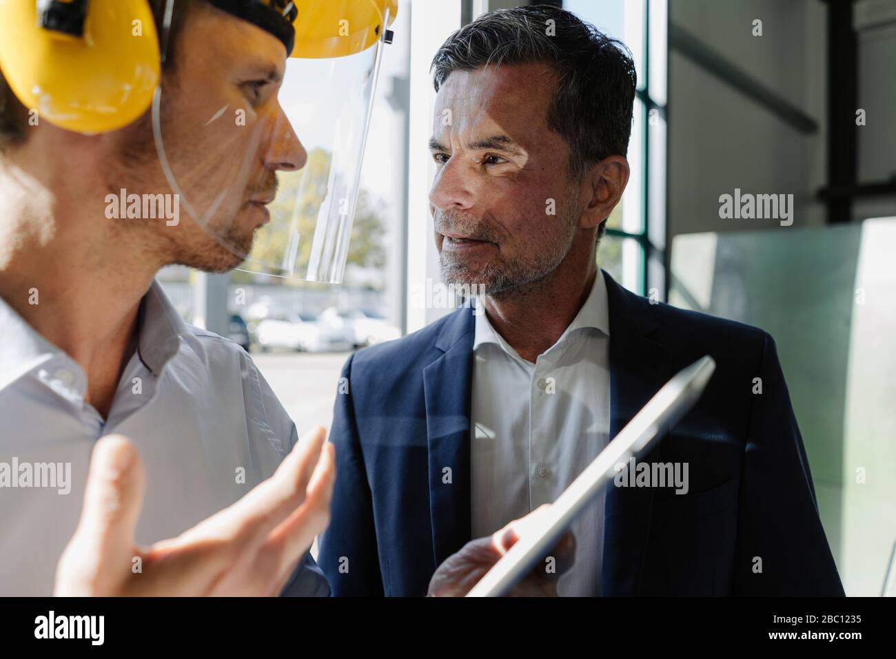 Businessman and man wearing safety helmet facing each other Stock Photo ...