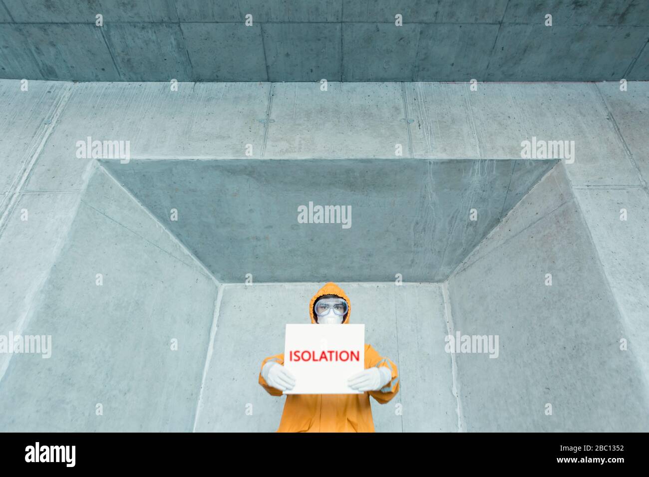 Portrait of man wearing protective clothing holding an 'isolation' sign ...