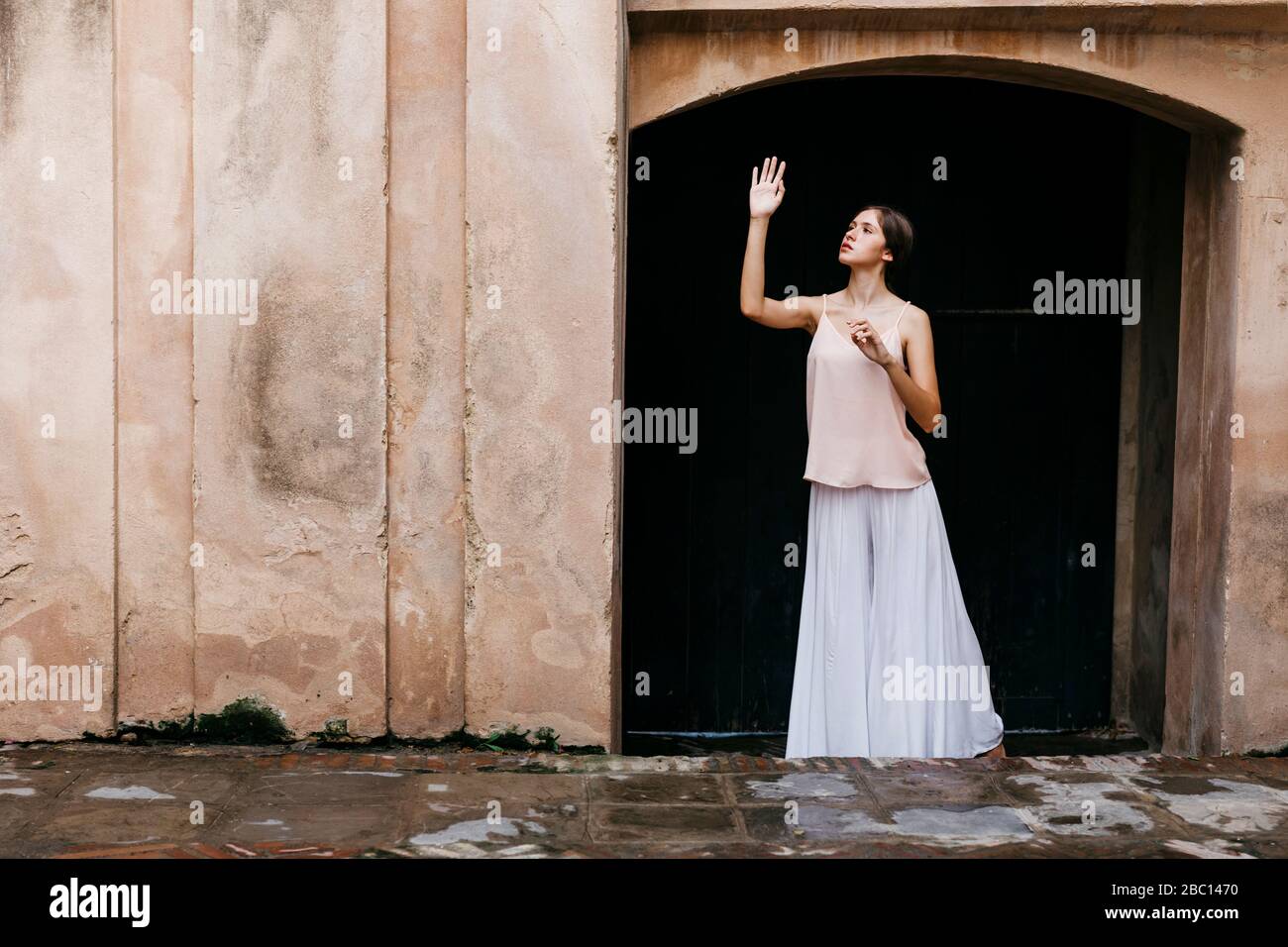 Delicate portrait of young girl in front of an old building with arms ...