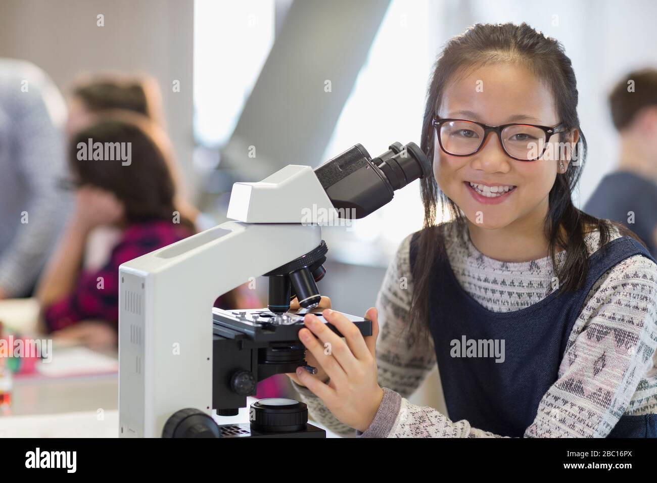Portrait smiling, confident girl student using microscope, conducting ...
