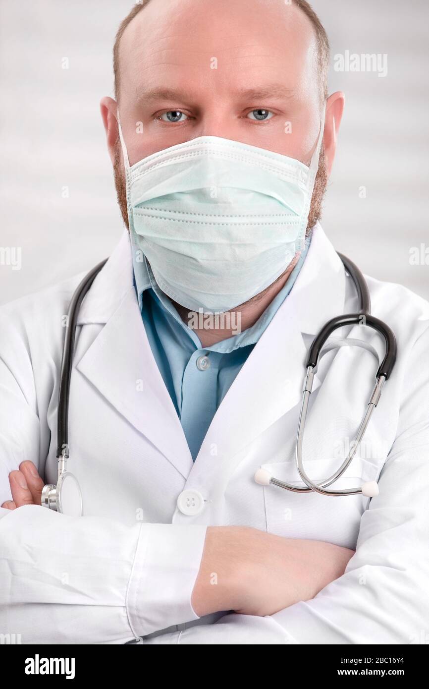 Portrait of a serious doctor wearing protective face mask and ...