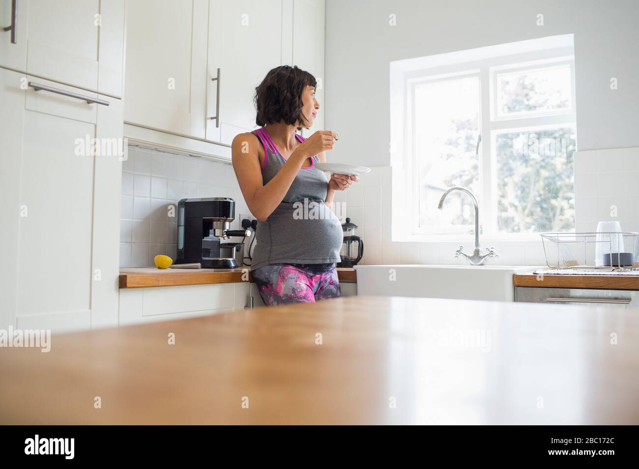 Thoughtful pregnant woman eating in kitchen looking out window Stock ...