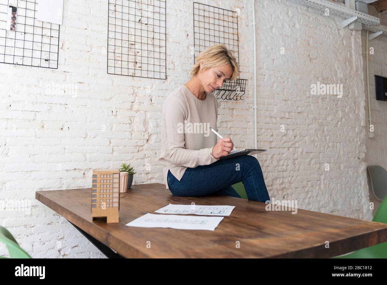 Mature woman at work sitting on desk in architectural office Stock ...