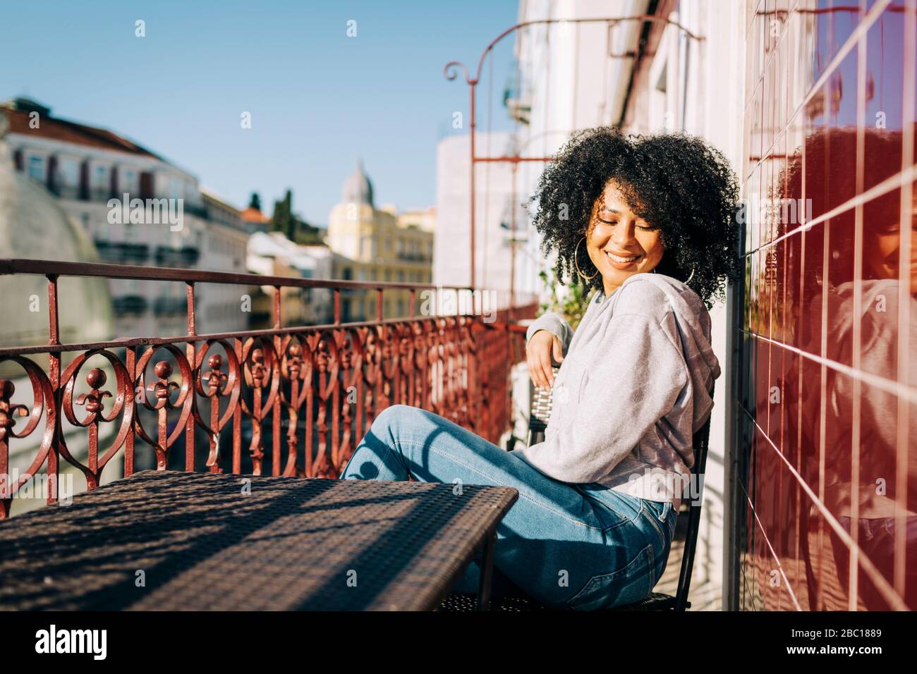Happy young woman with curly hair sitting on balcony enjoying the ...
