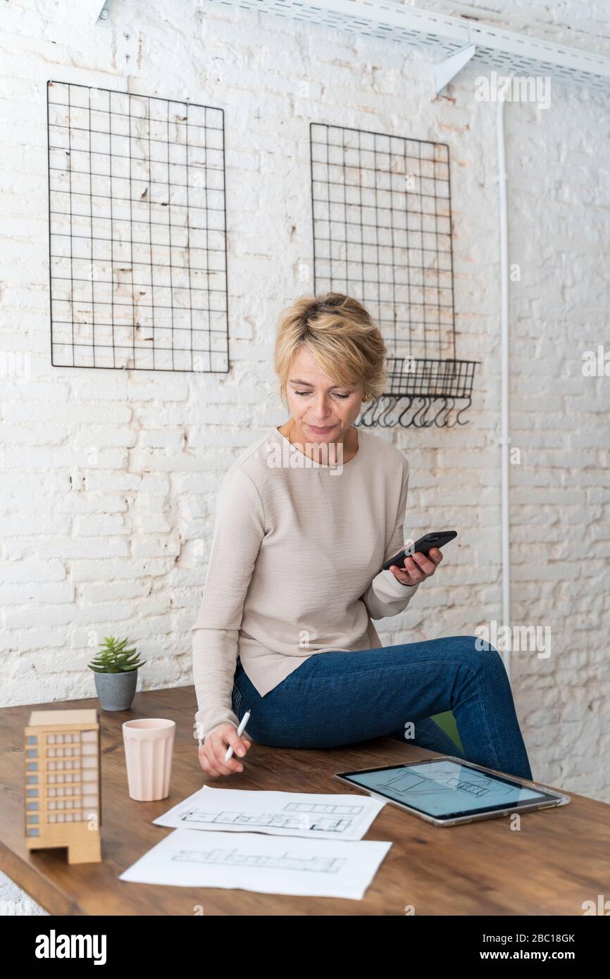 Mature woman at work sitting on desk in architectural office Stock ...