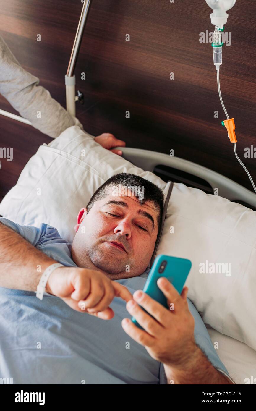 Patient lying in hospital bed using cell phone Stock Photo - Alamy