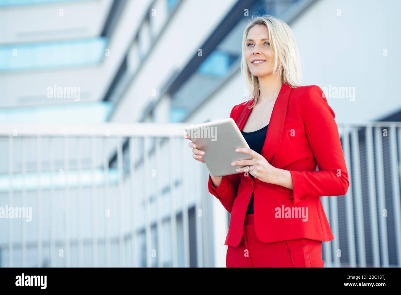 Blond businesswoman wearing red suit and using digital tablet at an ...