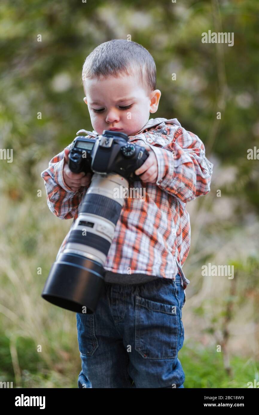 Portrait of toddler looking at digital reflex camera with big lens in ...