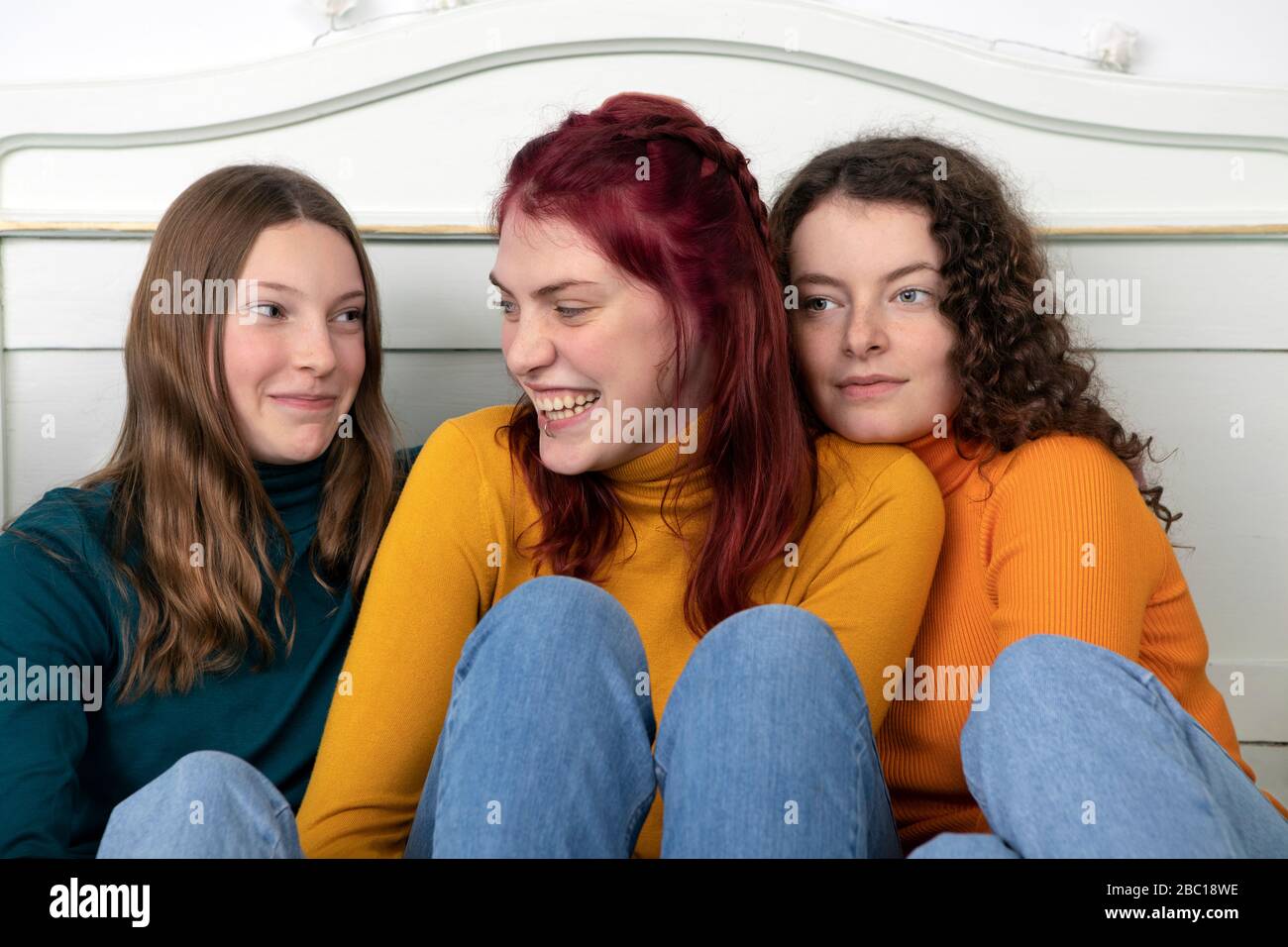 Portrait of three happy sisters sitting together on bed Stock Photo - Alamy