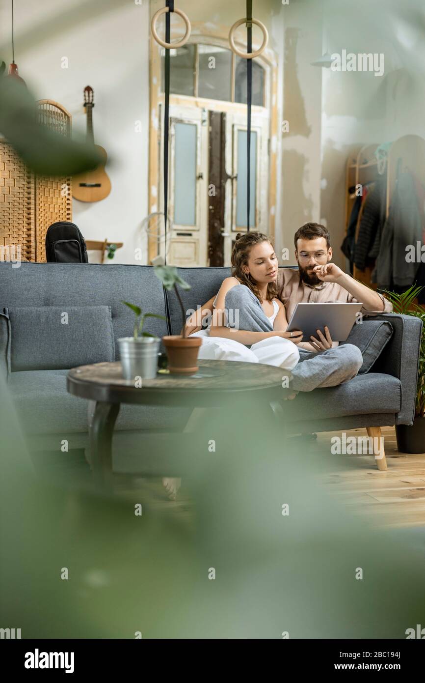 Young couple sitting on couch at home, using digital tablet Stock Photo ...