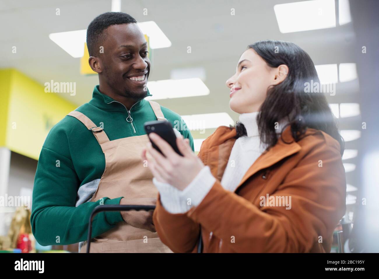 Grocer helping customer with smart phone in supermarket Stock Photo - Alamy