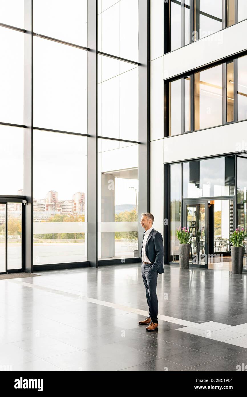 Successful businessman standing in entrance hall of office building ...