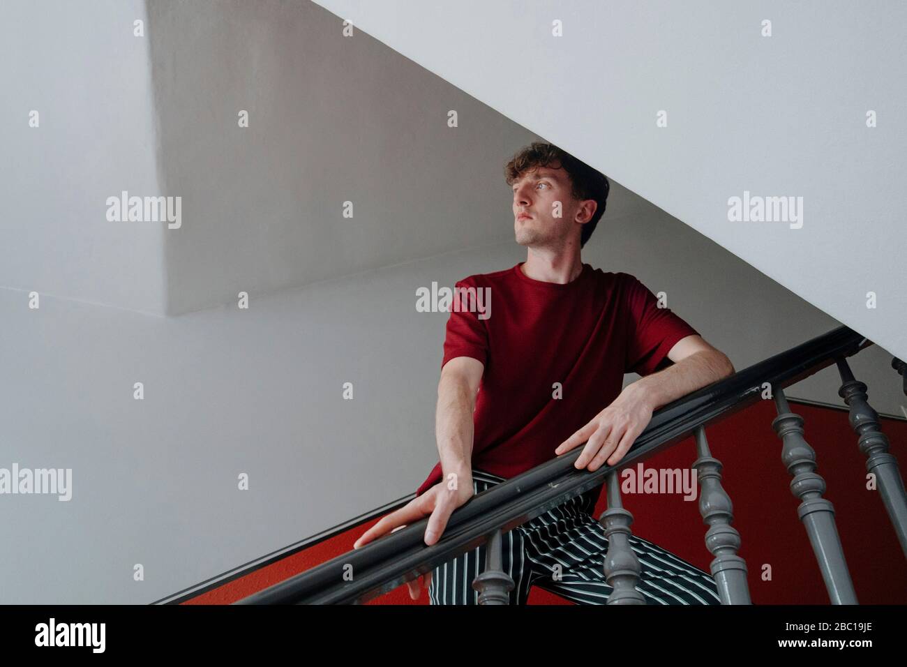 Serious young man leaning on banister looking at distance Stock Photo ...