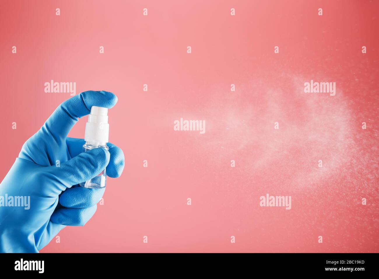 A blue-gloved hand holds a disinfectant on a pink background ...