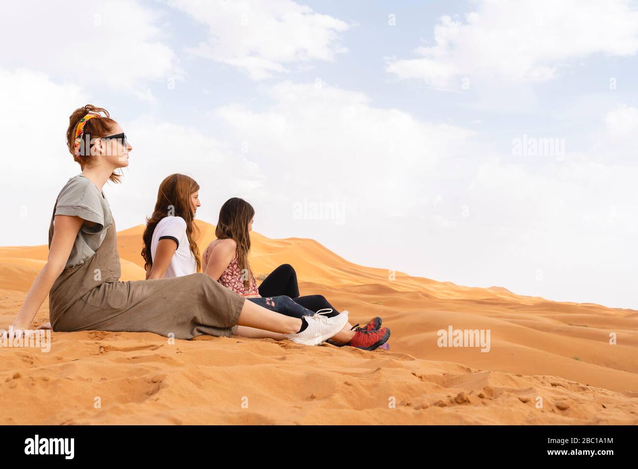 Three young women sitting in sand dune in Sahara Desert, Merzouga ...