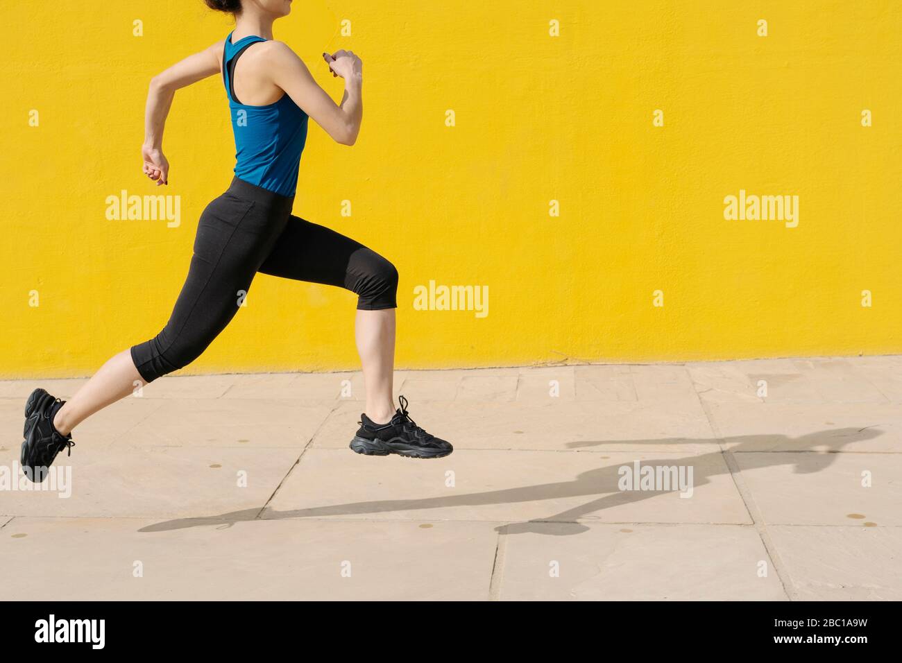 Young woman jogging in front of a yellow wall Stock Photo - Alamy