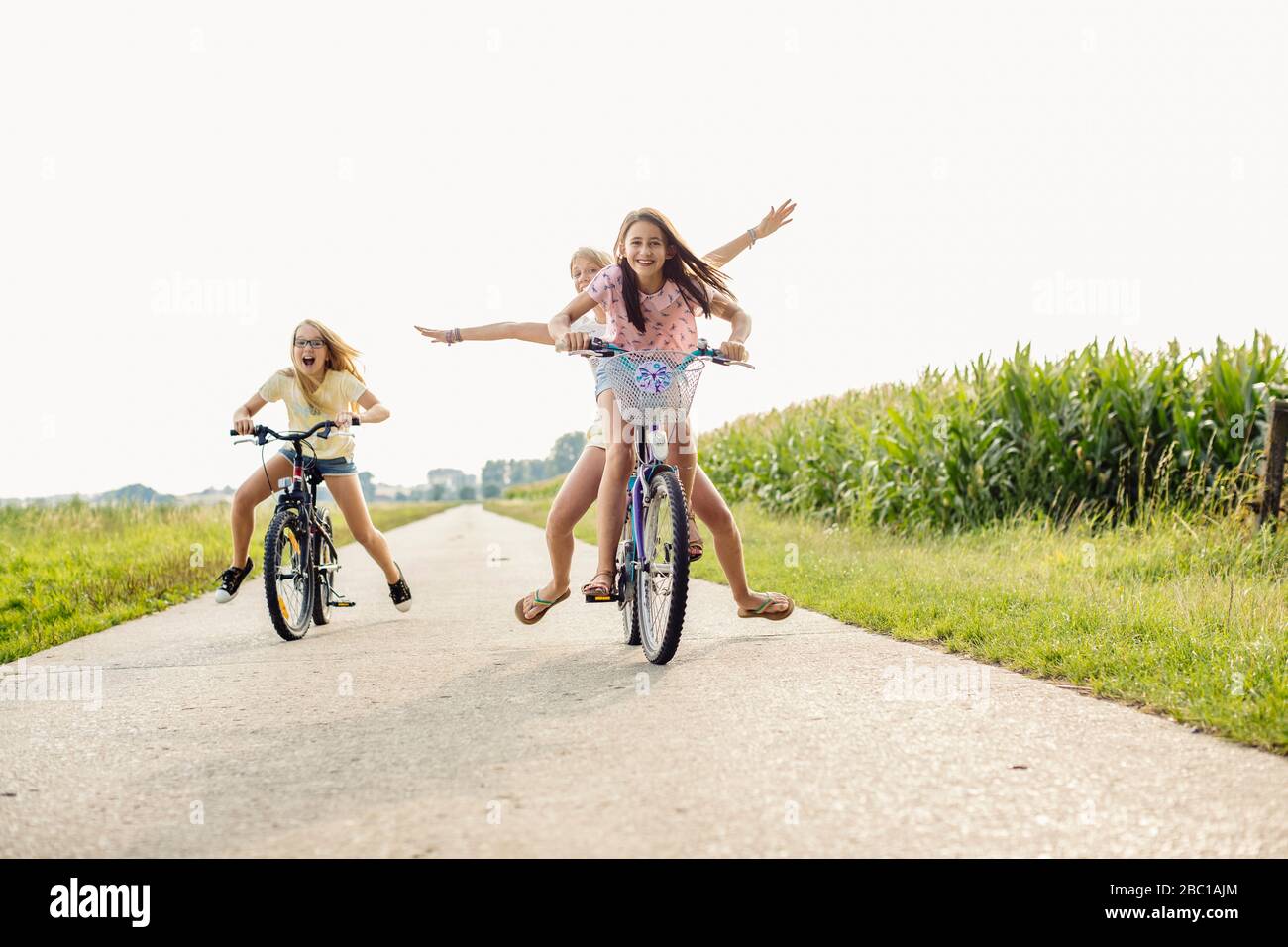 Happy girls riding bicycle on a country lane Stock Photo - Alamy