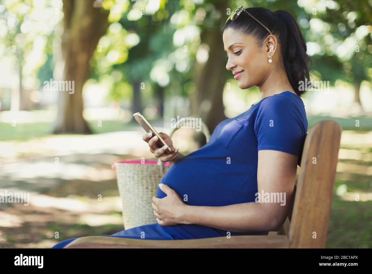 Pregnant woman texting with cell phone on park bench Stock Photo - Alamy