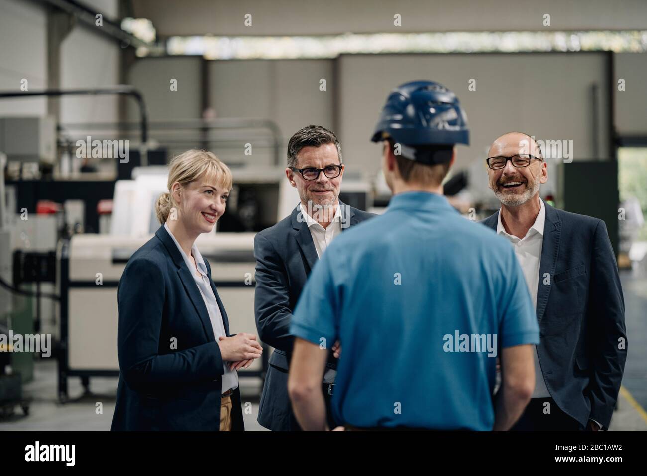 Smiling business people looking at worker in a factory Stock Photo - Alamy